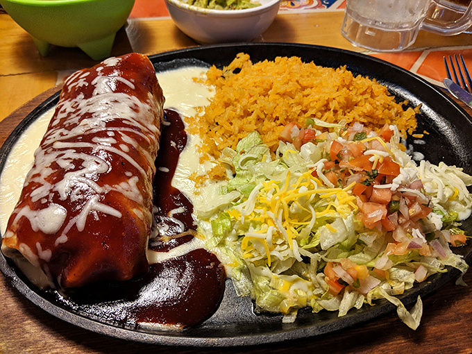 The chimichanga arrives sizzling on its wooden platform, cheese bubbling like lava, daring you to wait until it cools. Spoiler alert: you won't.