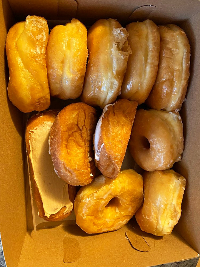 A dozen glazed donuts nestled in their cardboard cradle&mdash;like edible gold bars waiting to fund your happiness deficit.
