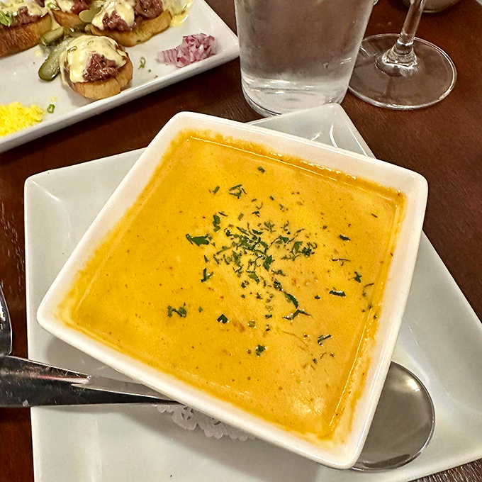 The crab bisque glows with promise, a golden pool of oceanic luxury that makes you want to abandon your spoon for a straw.