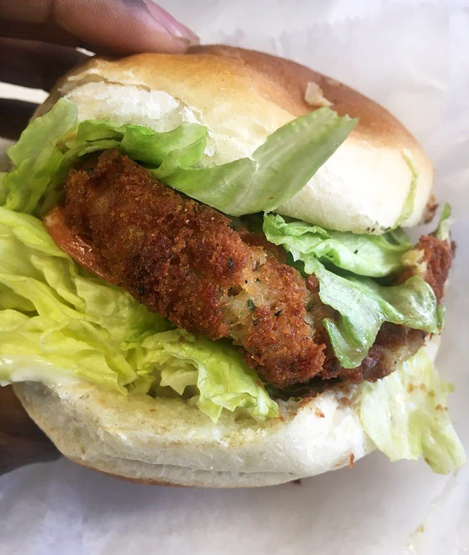 Behold the crab cake sandwich in its natural habitat—a golden-brown disk of seafood perfection nestled between pillowy bread.