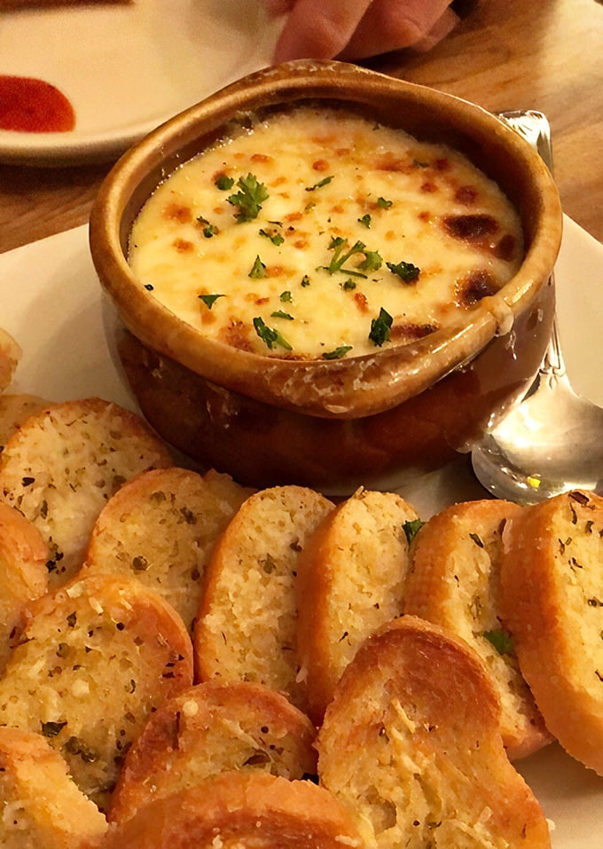The French onion soup arrives with a crown of melted cheese so perfect, it deserves its own coronation ceremony.