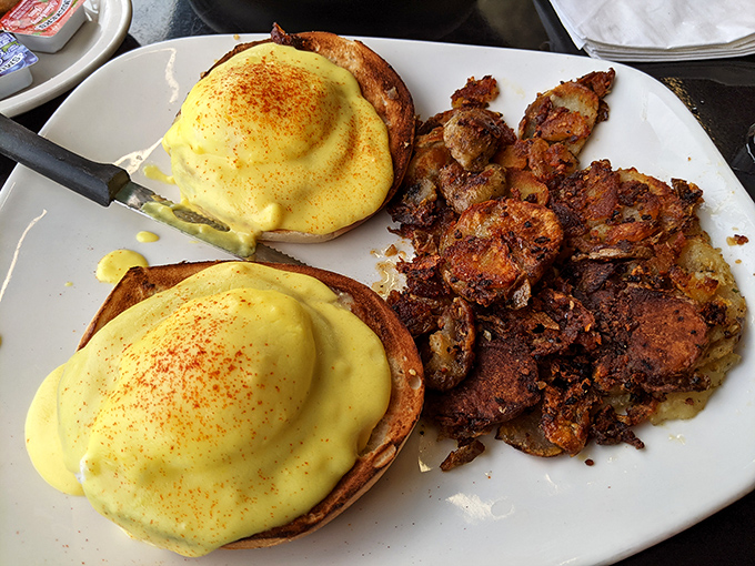 These eggs benedict aren't just breakfast, they're architecture—golden hollandaise cascading over perfectly poached eggs with crispy potatoes standing guard on the side.
