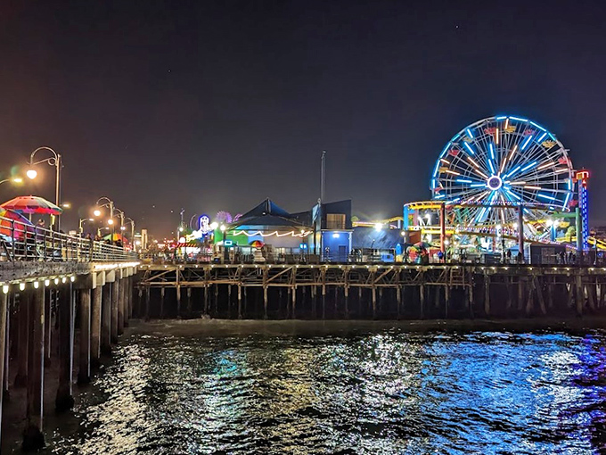 As daylight retreats, the pier transforms into an electric wonderland, painting the Pacific waters with dancing reflections of carnival lights.