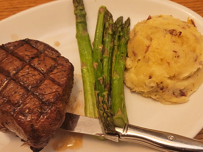 A perfectly cooked filet mignon flanked by vibrant asparagus and creamy mashed potatoes—the holy trinity of steakhouse perfection on a single plate.
