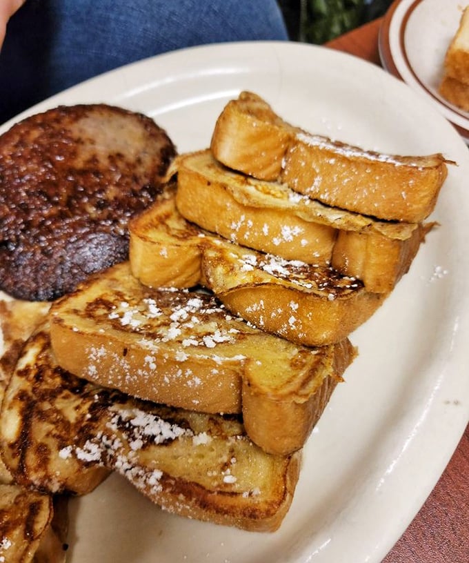 French toast stacked higher than your weekend ambitions, dusted with powdered sugar and served alongside a perfectly grilled breakfast meat.