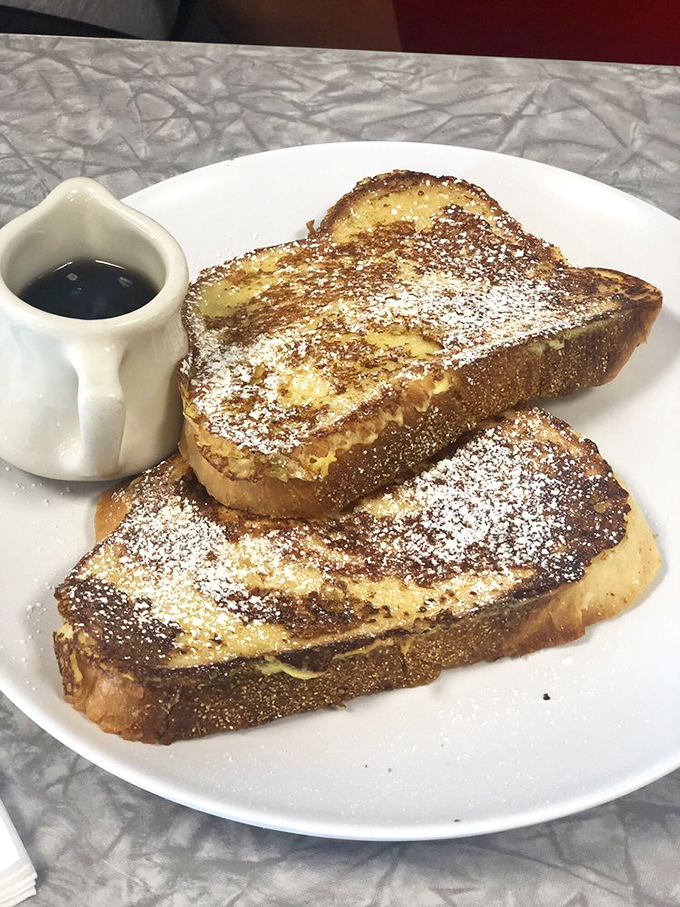 French toast that's dressed for success with a light dusting of powdered sugar. The tiny pitcher of syrup stands ready for the delicious flood to come.