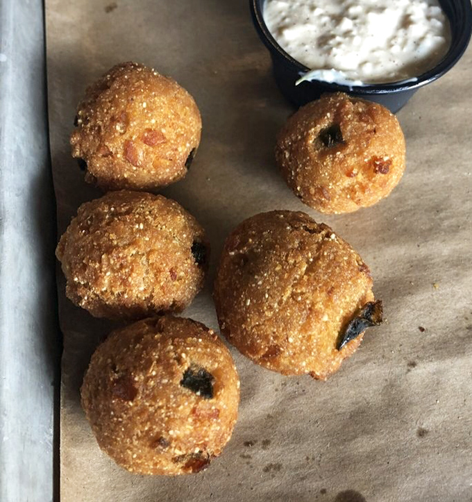 Golden-fried hush puppies that don't need to speak to make their point &ndash; crispy outside, tender inside, and ready for their dip in creamy sauce.