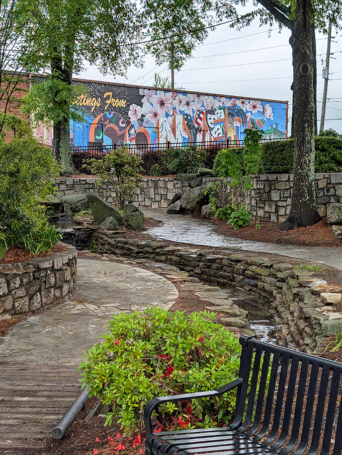 Nature and history intertwine at the Lewis Vaughn Botanical Garden, where stone pathways lead visitors past vibrant flowers beneath a striking mural backdrop.