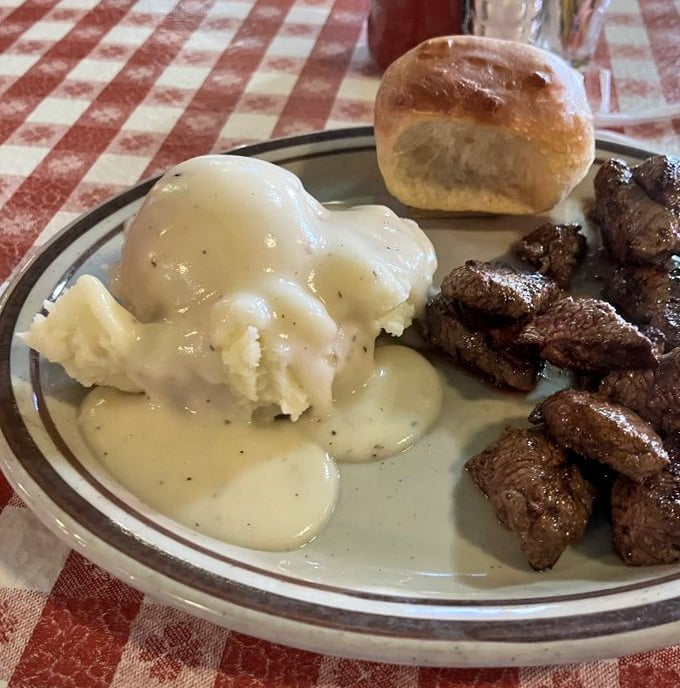 Comfort on a plate &ndash; creamy mashed potatoes swimming in gravy alongside perfectly seared steak bites, with a biscuit standing sentry.