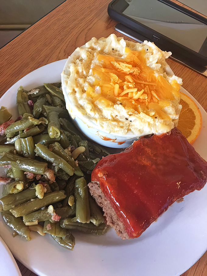 Southern comfort on a plate: meatloaf glazed to perfection, green beans with a story to tell, and mashed potatoes that could make a grown person weep.