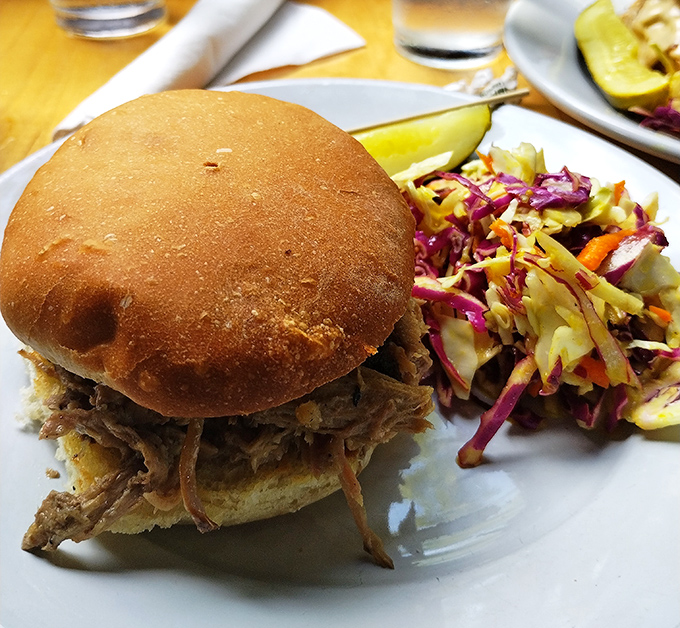 The pulled pork sandwich that launched a thousand road trips. Tender, smoky meat on a fresh-baked bun with vibrant slaw that cuts through the richness like a well-timed punchline.