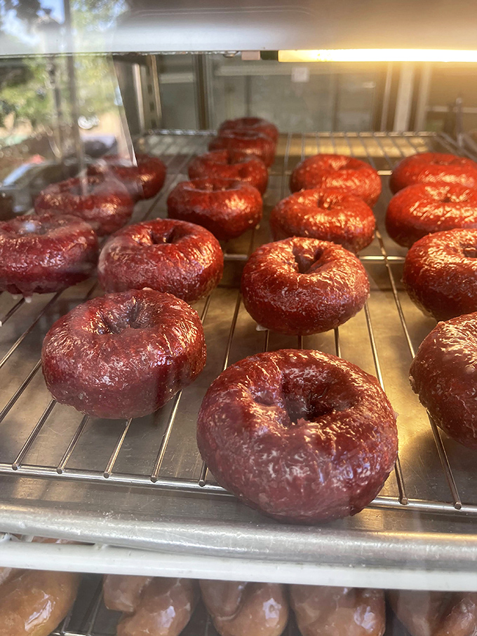 Red velvet donuts glisten like rubies in a bakery crown. Their deep crimson hue promises a cocoa-tinged indulgence that delivers.