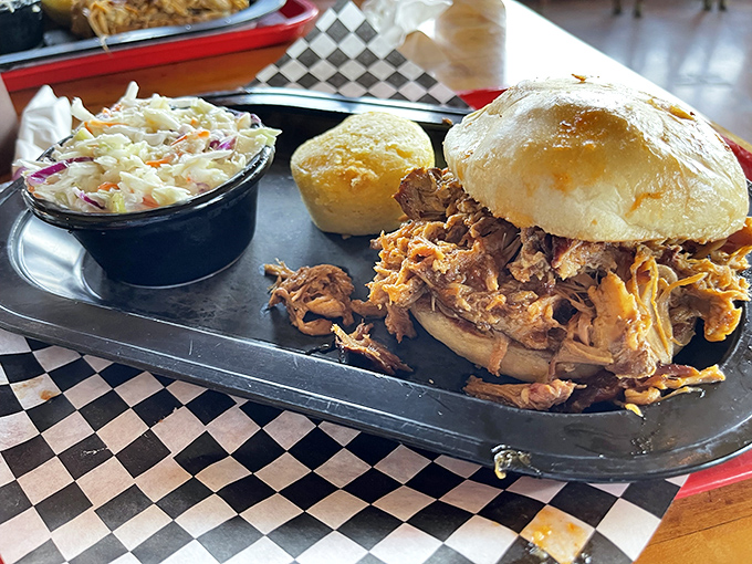 The pulled pork sandwich arrives like a meaty mountain between buns, with coleslaw standing guard and a cornbread sidekick ready for action.