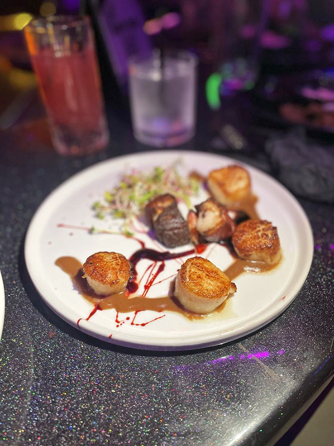 Perfectly seared scallops arrive like edible jewels against a canvas of artistic sauce drizzles. 