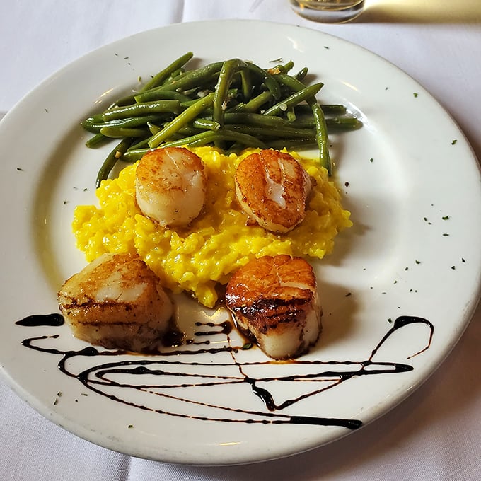 Seared scallops perched atop sunshine-yellow risotto like culinary royalty. The artistic balsamic drizzle isn't just for show &ndash; it's the perfect acidic counterpoint.