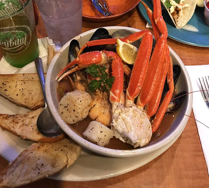 Seafood nirvana in a bowl! Crab legs reaching skyward like they're trying to escape, surrounded by mussels, scallops, and crusty bread for sopping up that glorious broth.