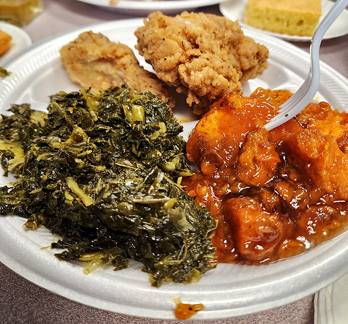 Southern trinity on full display: perfectly seasoned collard greens, sweet candied yams, and fried chicken that would make your grandmother both proud and jealous.