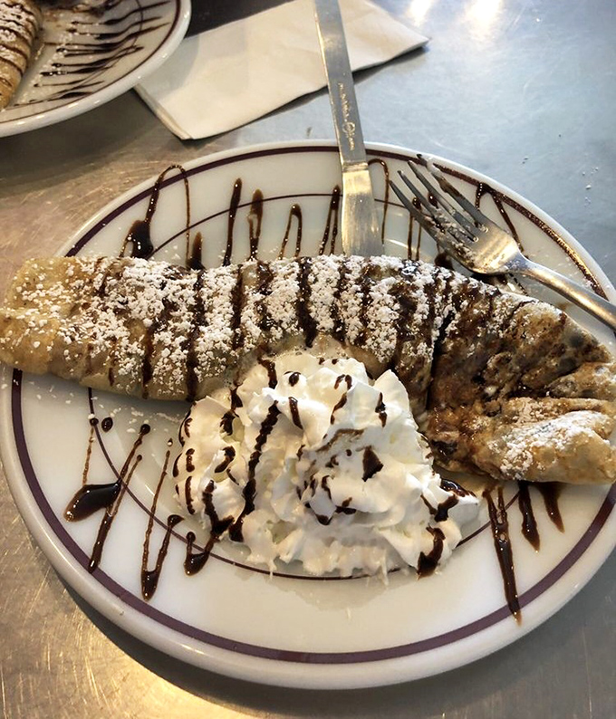 Chocolate drizzle performing an interpretive dance across whipped cream and a perfectly folded crepe. Dessert or art installation? Both.