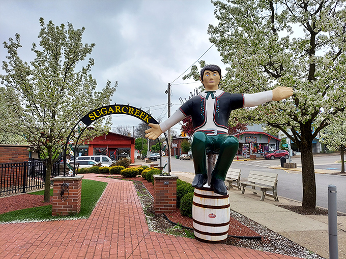 Not your average town greeter! This wooden Swiss figure perched atop a barrel welcomes visitors with open arms under flowering trees &ndash; no yodeling required.