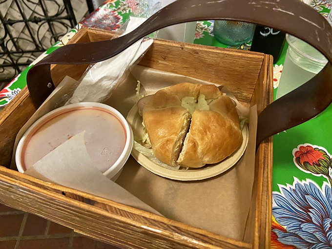 Not just any croissant&mdash;this golden vessel cradles what appears to be turkey, served in a rustic wooden carrier that somehow makes everything taste better.