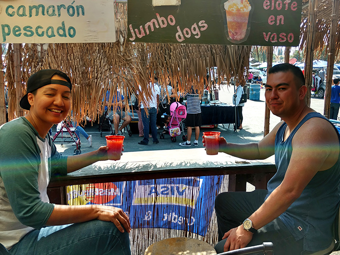 A thatched-roof refreshment stand offers the perfect pit stop&mdash;colorful drinks in hand, these shoppers have mastered the art of swap meet hydration.