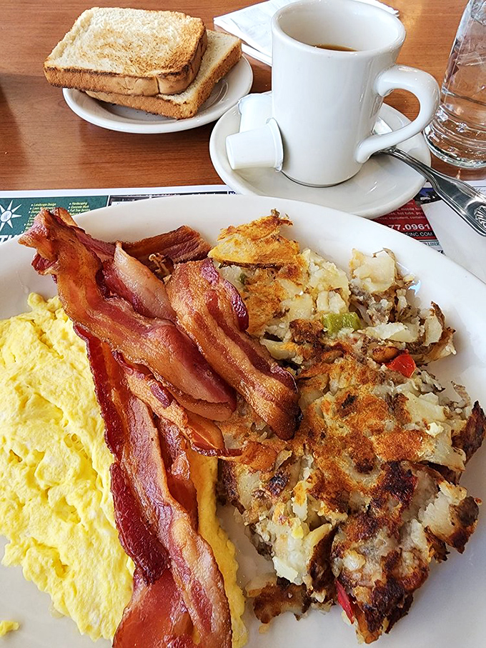 The holy trinity of breakfast perfection: fluffy scrambled eggs, crispy home fries with just the right seasoning, and bacon that shatters like caramelized dreams.