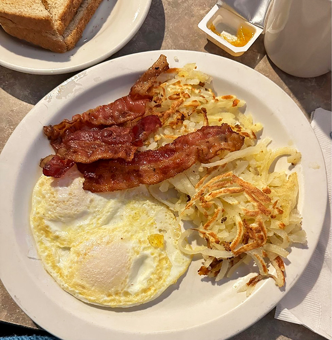 The breakfast trinity: perfectly cooked eggs, bacon with the ideal crisp-to-chew ratio, and hash browns that crackle with each forkful.