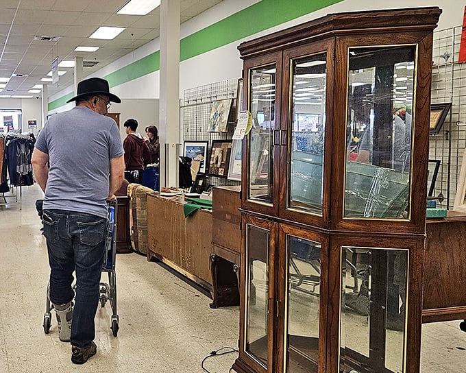 A shopper examines a wooden display cabinet, contemplating whether this might be the perfect home for their collection of miniature spoons.
