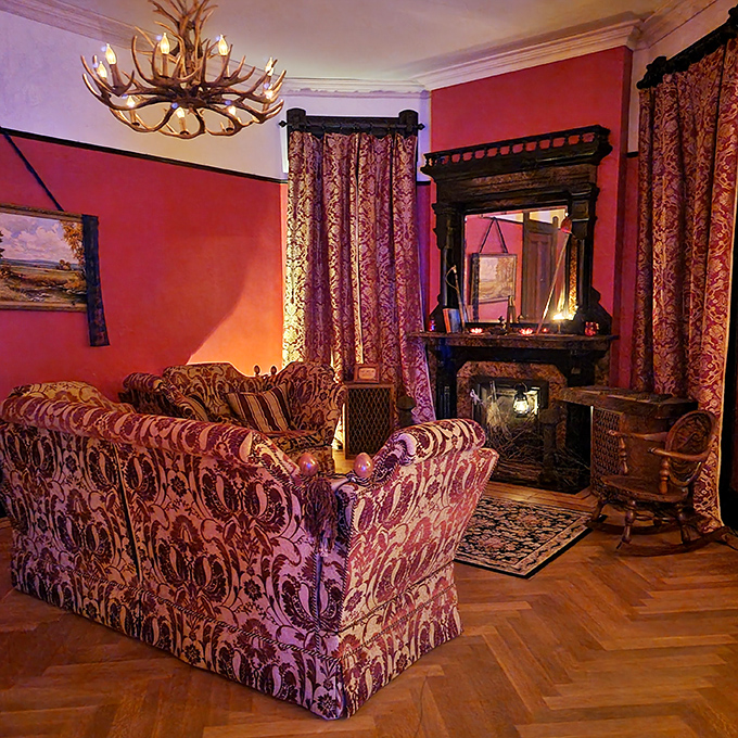 The antler chandelier casts dramatic shadows across rich red walls, creating the perfect ambiance for telling ghost stories or planning elaborate dinner parties.