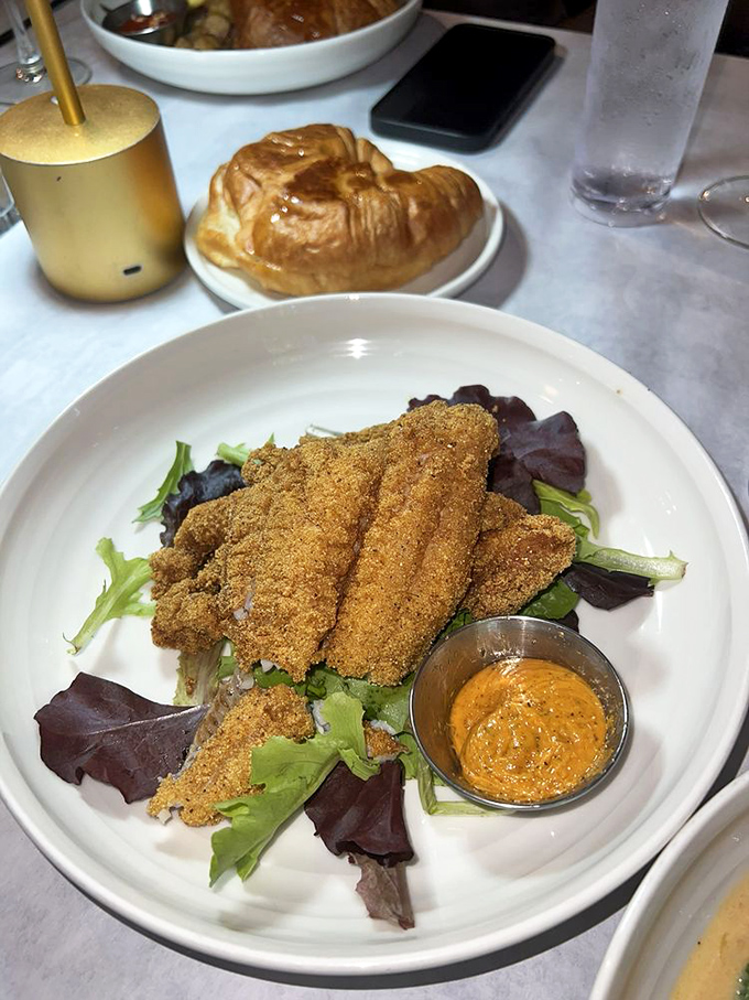 Golden-crusted catfish perched atop fresh greens with a side of remoulade that's begging to be introduced to every bite.