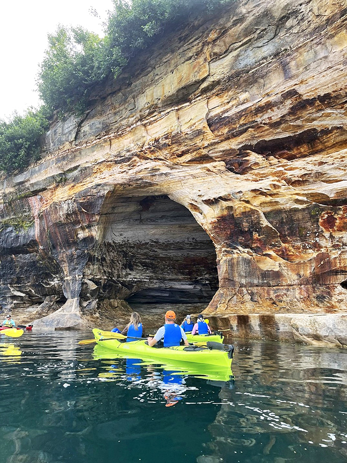 Kayakers pause beneath a natural stone cathedral, their bright vessels providing perfect scale for the massive, mineral-stained archways carved by millennia of waves.
