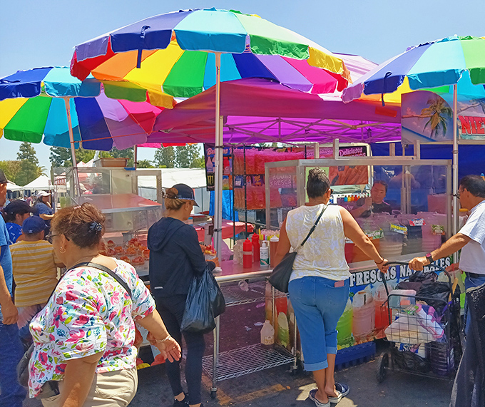 Rainbow umbrellas shield a gathering of snack enthusiasts from the California sun while fresh fruit cups become portable works of art.