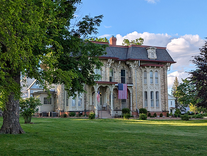 The stately Amos Gould House proudly displays its American flags, a limestone testament to Victorian elegance that's survived over a century of Michigan seasons.