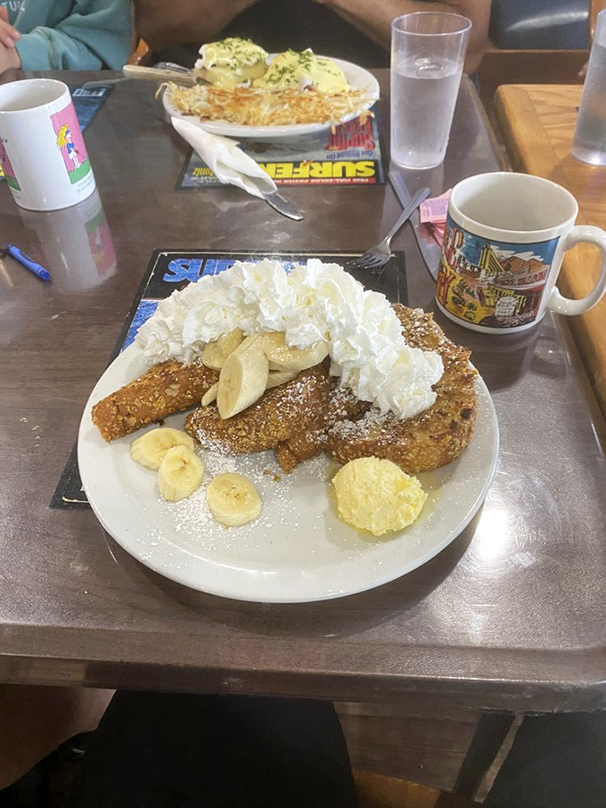 Banana Crunch French Toast arrives like a breakfast carnival, complete with whipped cream mountains and banana slices standing in as delicious spectators.