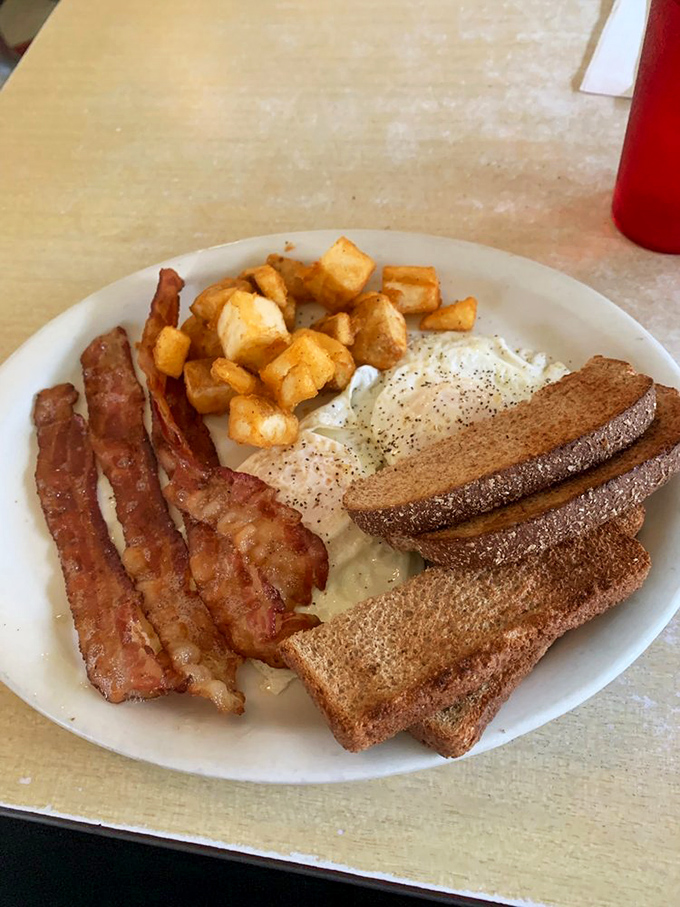 Breakfast perfection in its purest form: crispy bacon, golden toast, eggs, and home fries arranged like the four corners of a delicious universe.