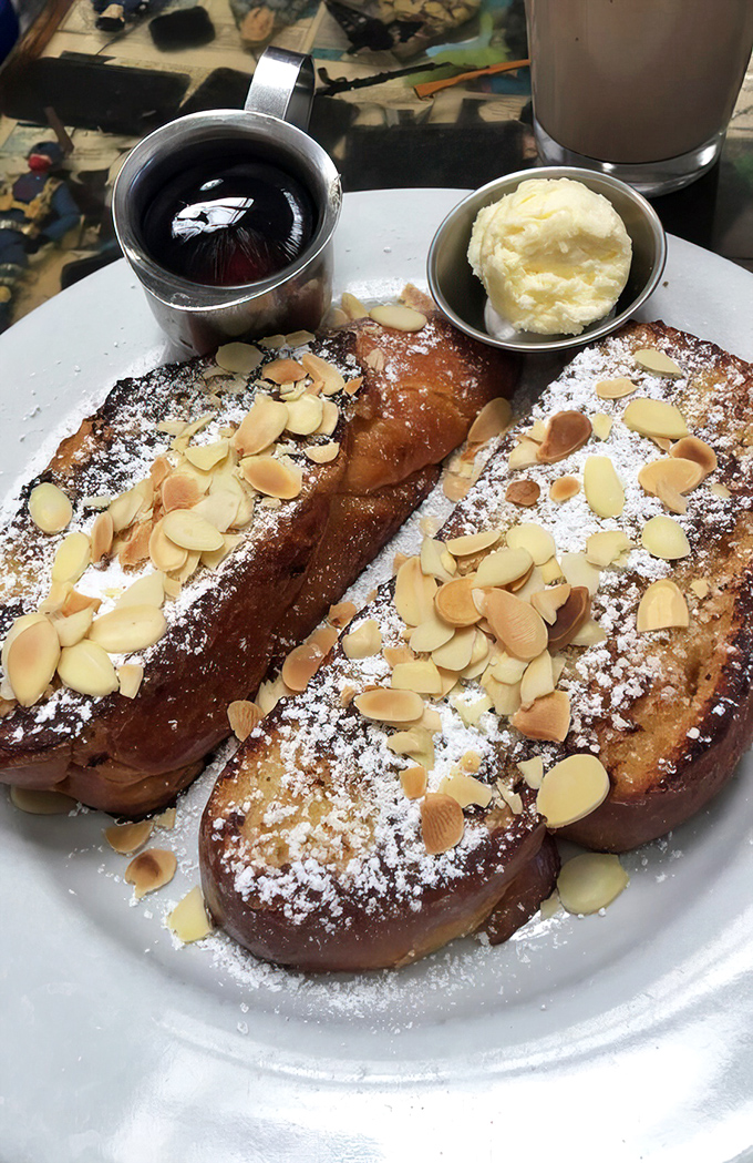 French toast that deserves its own fan club&mdash;golden-brown challah bread topped with powdered sugar and almonds, ready for its maple syrup bath.