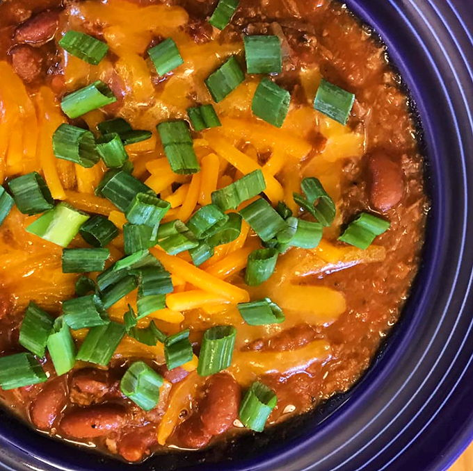 A bowl of hearty chili that doesn't just warm your stomach but hugs your soul, topped with melted cheddar and green onions.