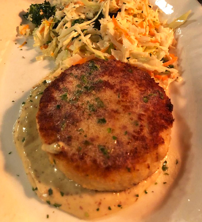 This crab cake isn't playing games—golden-crusted perfection atop a canvas of sauce that would make even non-seafood lovers reconsider their life choices.