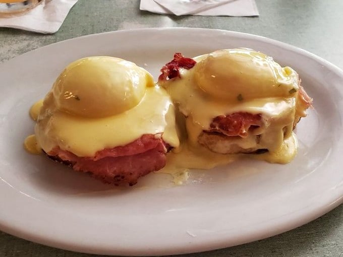 Eggs Benedict reimagined: perfectly poached eggs perched atop ham, draped in hollandaise that cascades like a buttery waterfall.