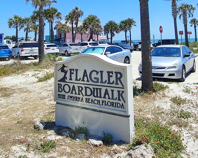 The Flagler Boardwalk sign stands sentinel to beach bliss, promising sandy memories just beyond those swaying palms and parked sedans.