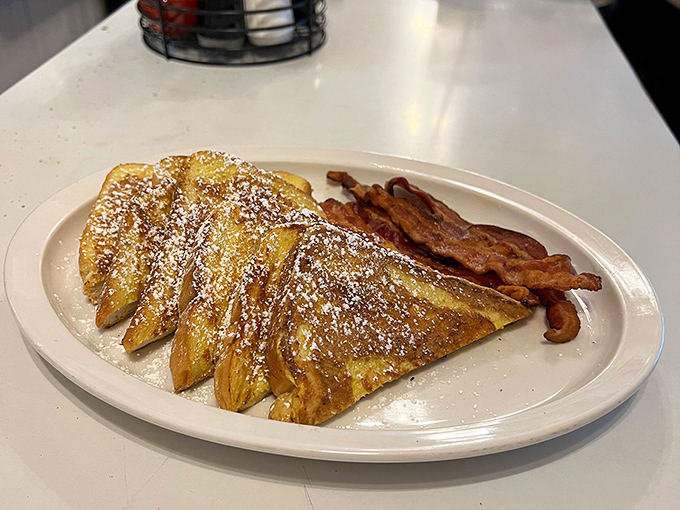 French toast dusted with powdered sugar like fresh snow on Christmas morning, paired with bacon that's achieved that mythical balance between crispy and chewy.