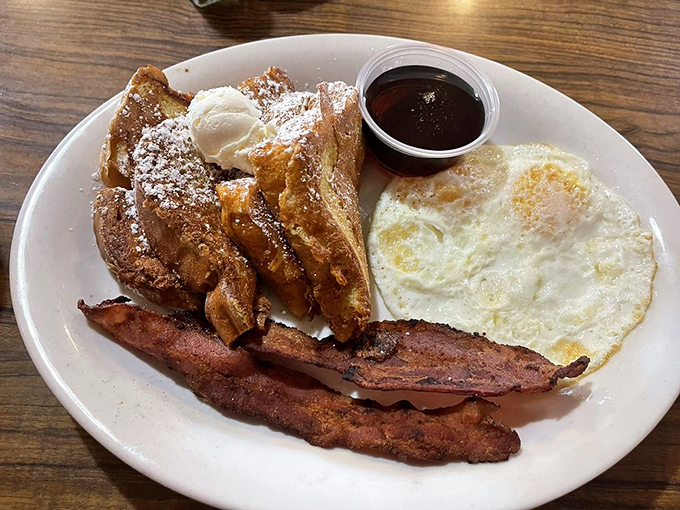The legendary French toast arrives dusted with powdered sugar like fresh snow on a perfect morning. This plate explains why breakfast is worth getting out of bed for.
