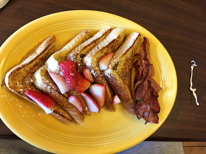 The breakfast trifecta: pillowy French toast, ripe strawberries, and perfectly crisped bacon. Morning salvation on a sunshine-yellow plate.