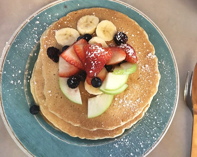 Pancakes wearing fruit like fine jewelry. The powdered sugar snowfall is Mother Nature's way of blessing your breakfast choices.
