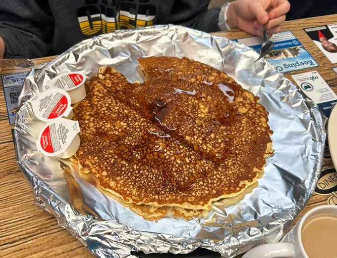 Pancakes so magnificent they require their own silver stage. The syrup pools in those perfect little bubbles, creating tiny lakes of maple goodness.