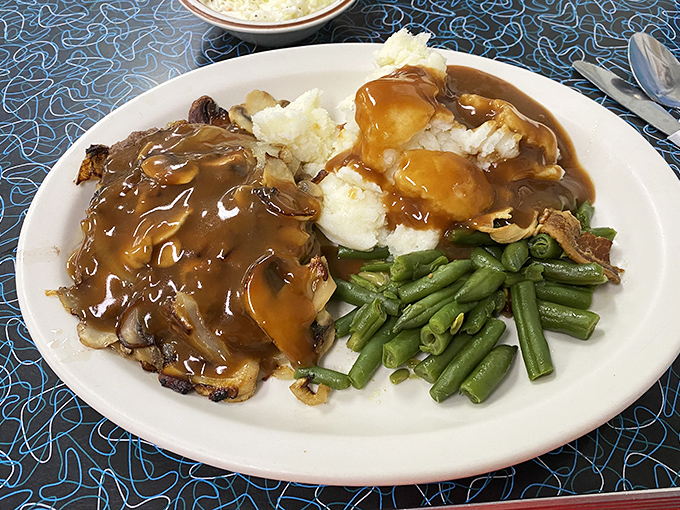 Comfort food royalty: meatloaf crowned with gravy alongside perfectly seasoned green beans and fluffy mashed potatoes.