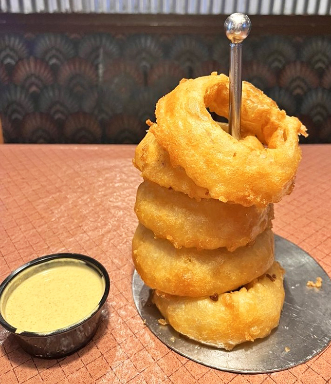 Onion rings stacked like delicious golden halos, with a dipping sauce that might make you forget your table manners.