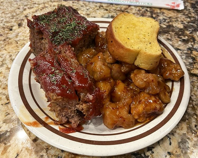 The holy trinity of comfort food: meatloaf glistening with tangy sauce, orange chicken in all its sweet-savory glory, and garlic bread&mdash;because carbs complete any buffet pilgrimage.