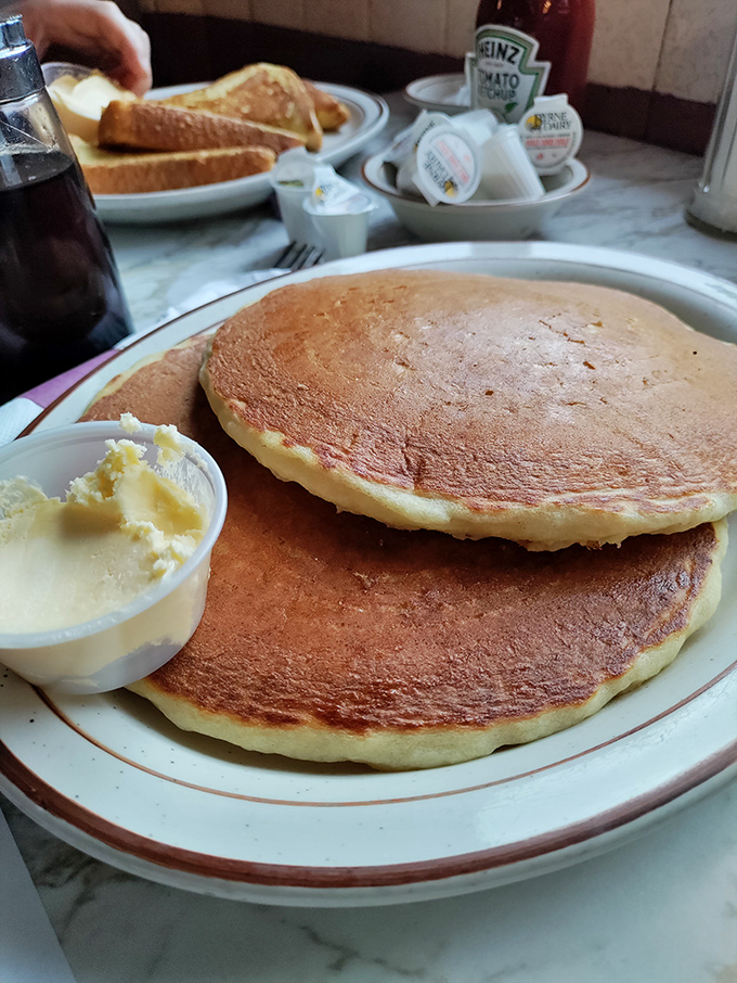 Pancakes so perfectly golden they belong in Fort Knox, with butter melting into those fluffy layers like a warm embrace.