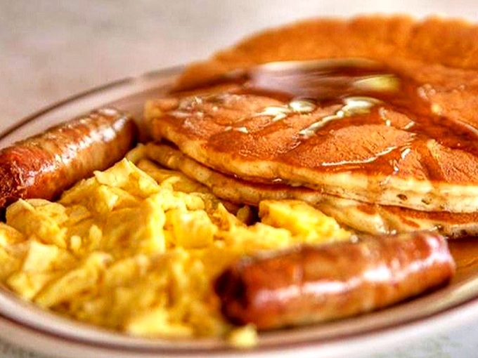 Golden pancakes glistening with butter and syrup, flanked by eggs and sausage. The breakfast trinity that's worth setting an alarm for.